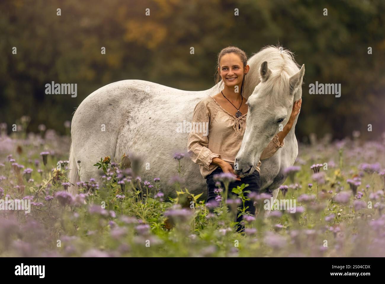 A young woman and her white horse gelding cuddling at a wildflower ...
