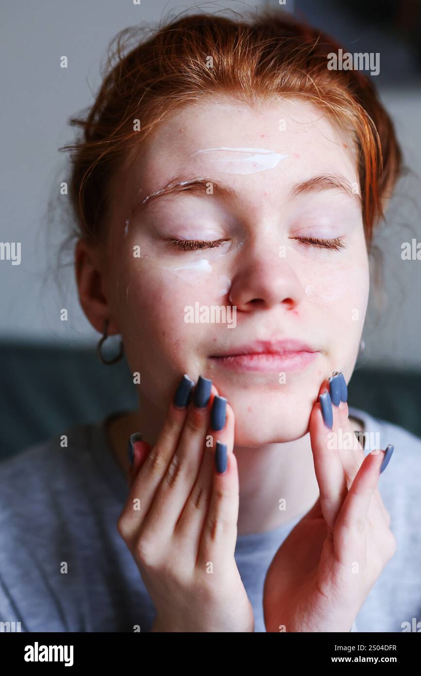Girl caring of her beautiful skin on the face. Applying moisturizer on ...