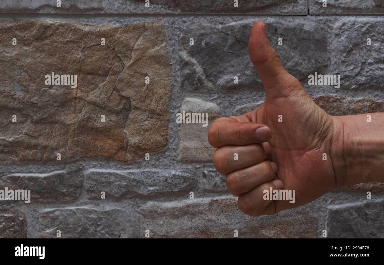 Close-up of a human hand giving a thumbs up against a varied stone wall ...