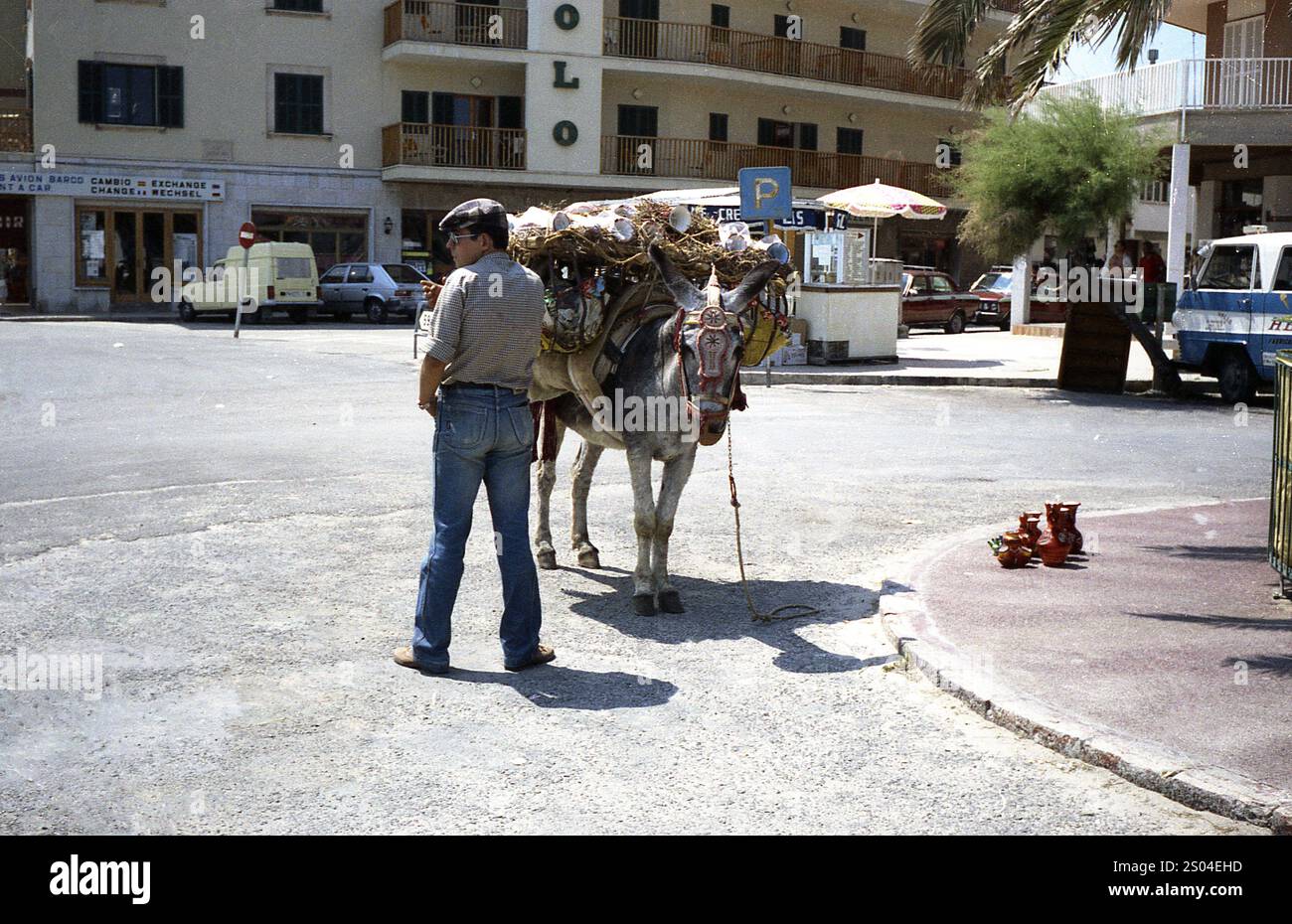 1982, a male street seller standing with his donkey carrying a range of ...