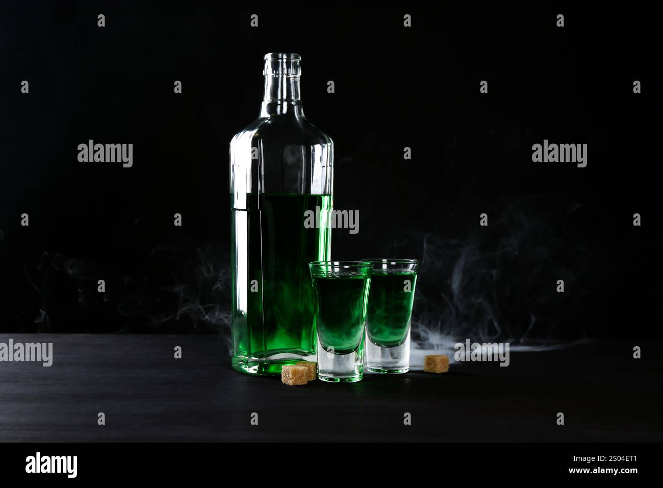 Absinthe in shot glasses, bottle and brown sugar on table against black ...