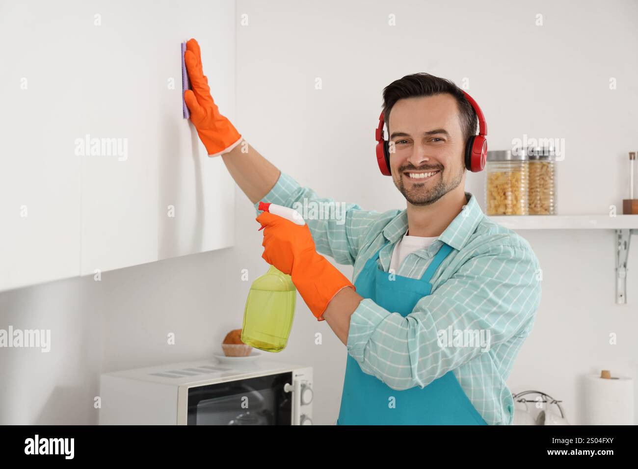 Male janitor with headphones cleaning cupboard in kitchen Stock Photo ...