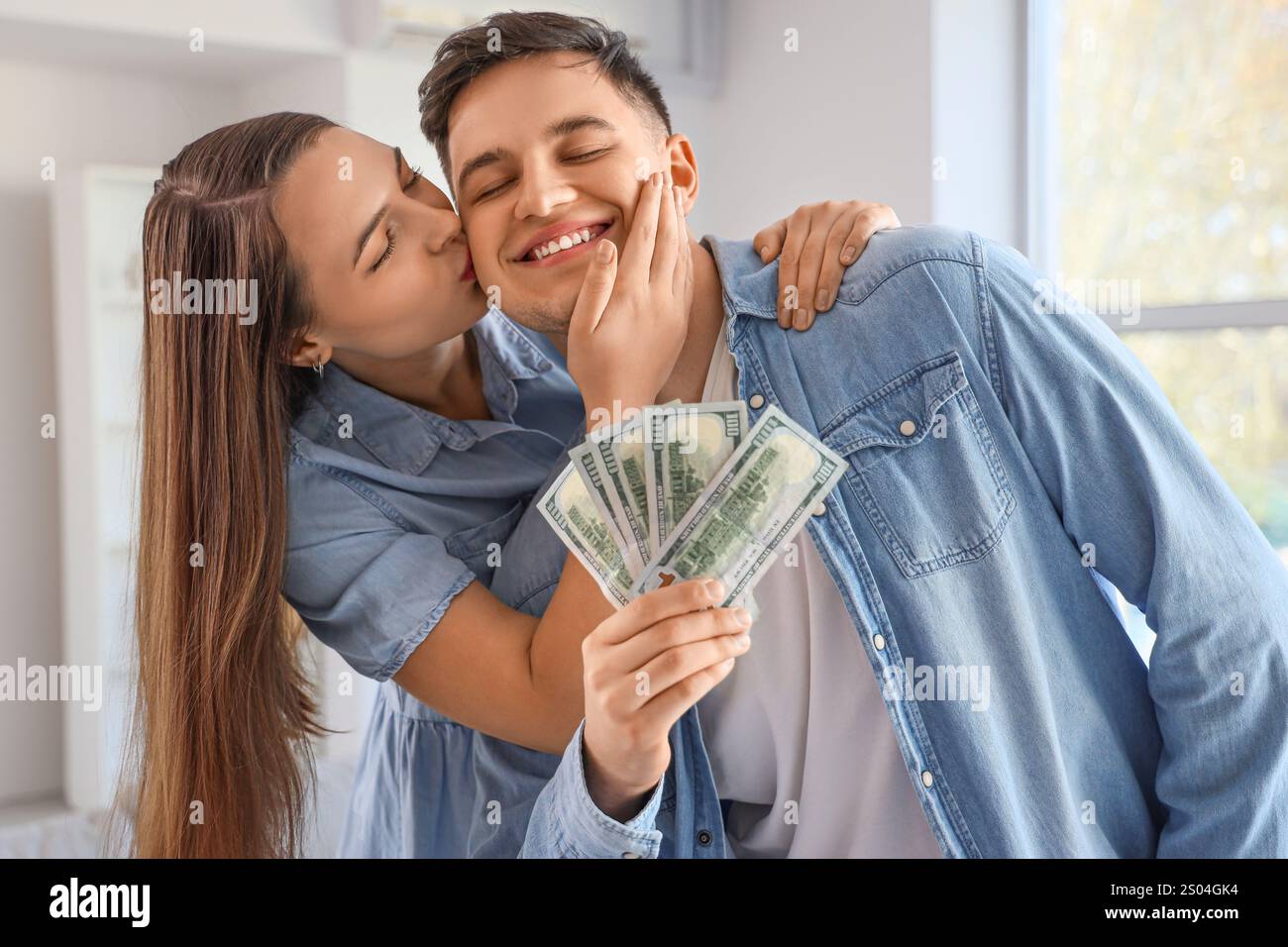 Young woman kissing her husband with money at home Stock Photo - Alamy