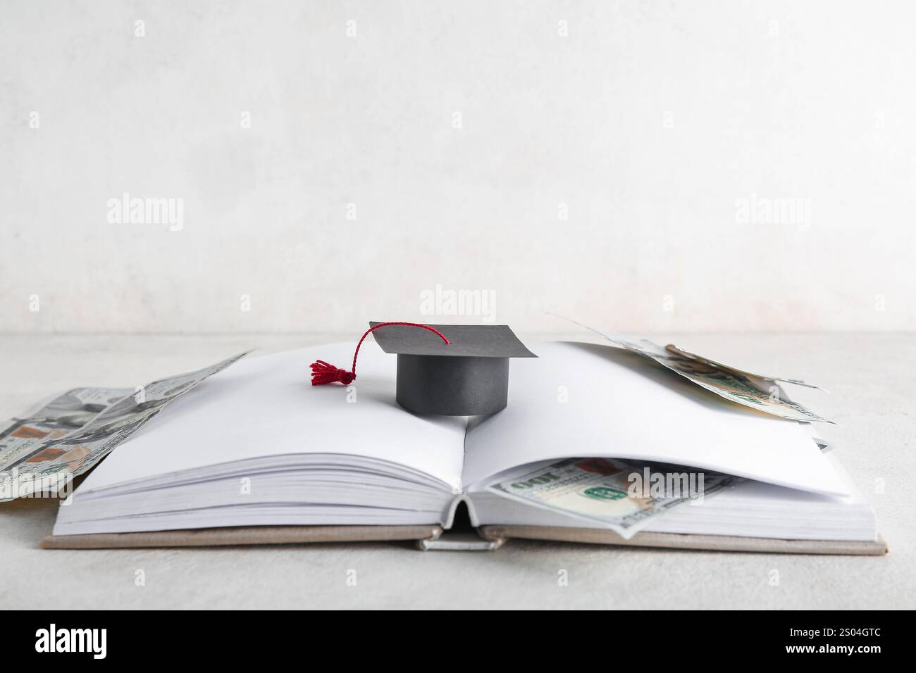 Open book, small graduation hat and dollar banknotes on light ...
