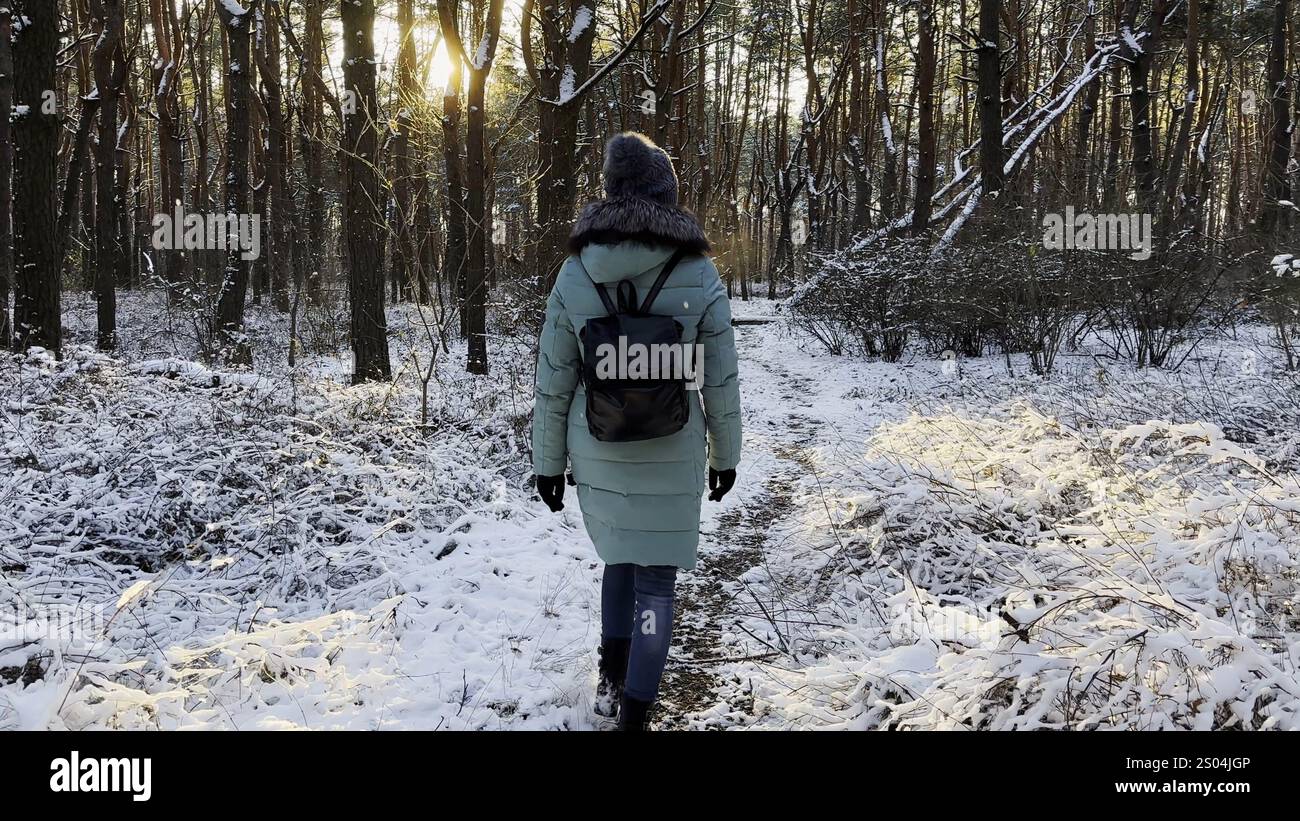 Young woman walking along path in sunny snowy forest. Girl with ...