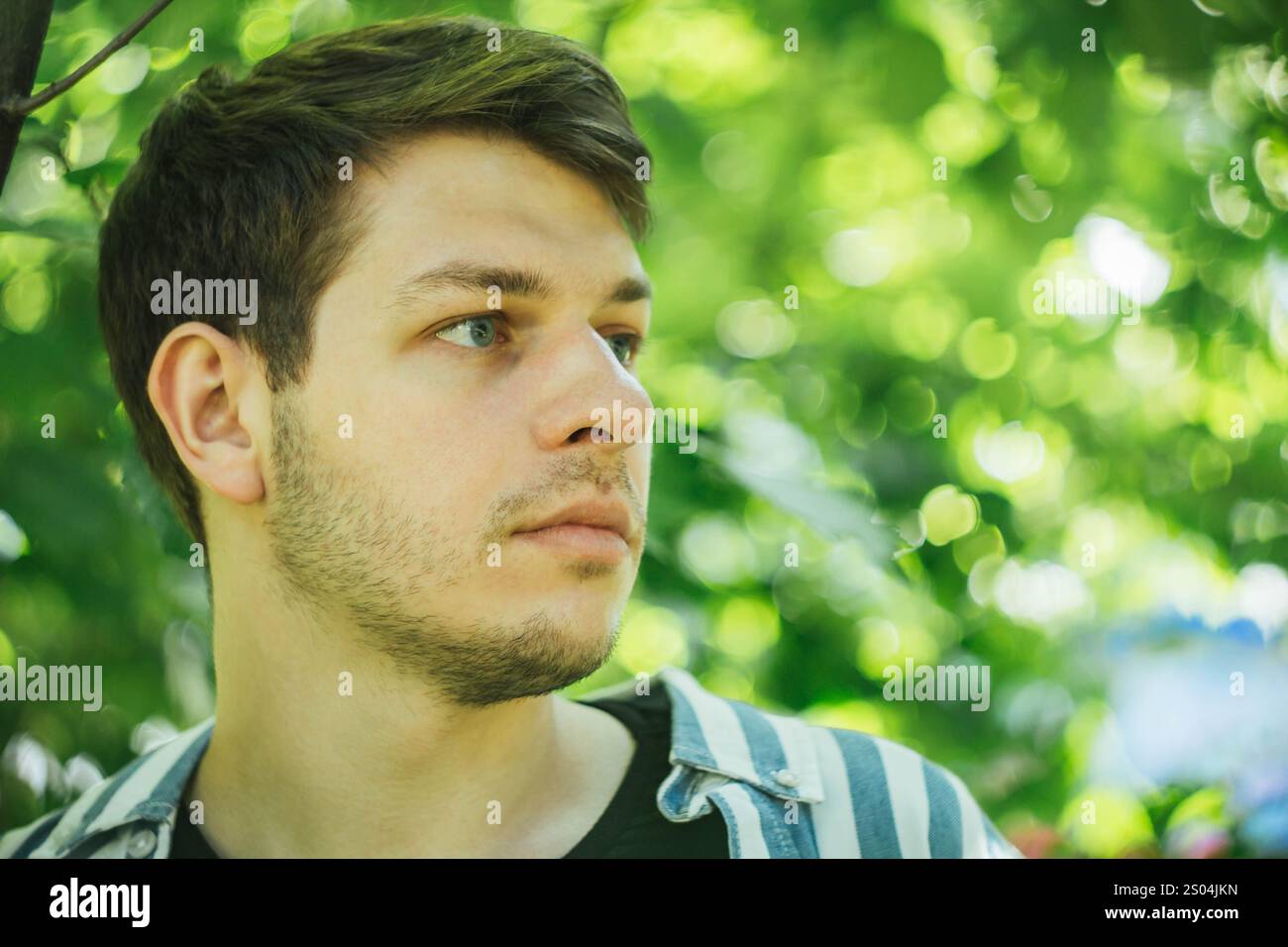 A young man stands in the middle of green nature, his face close-up ...