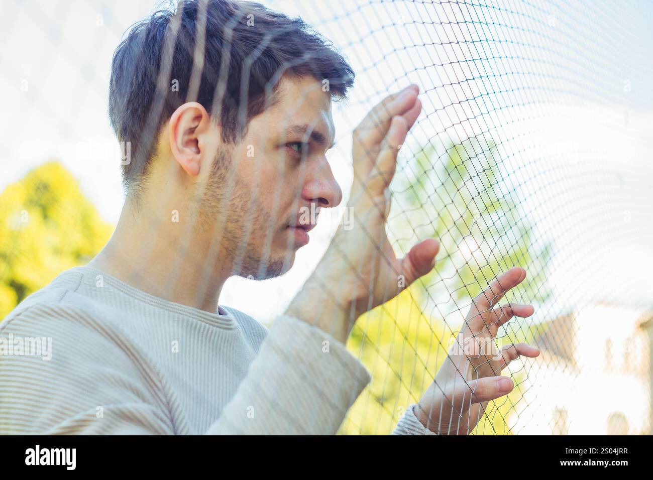 A young man with a stern expression peers through the mesh. The ...