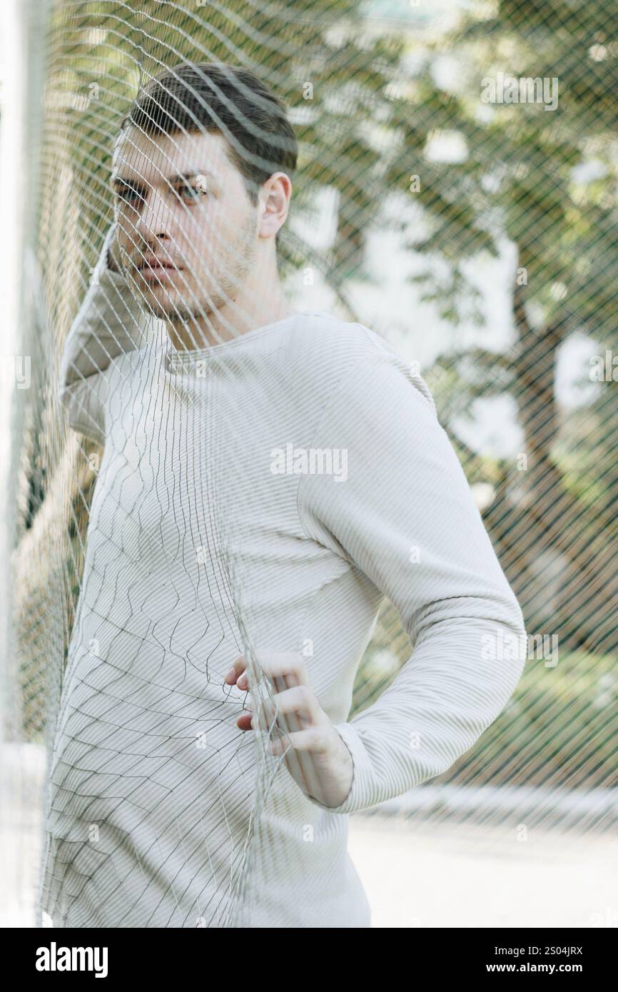 A young man with a stern expression peers through the mesh. The ...