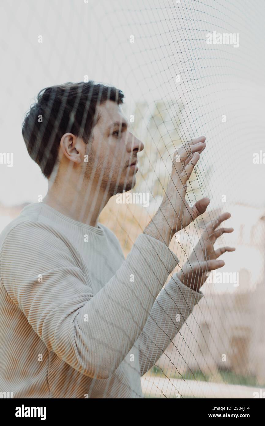 A young man with a stern expression peers through the mesh. The ...