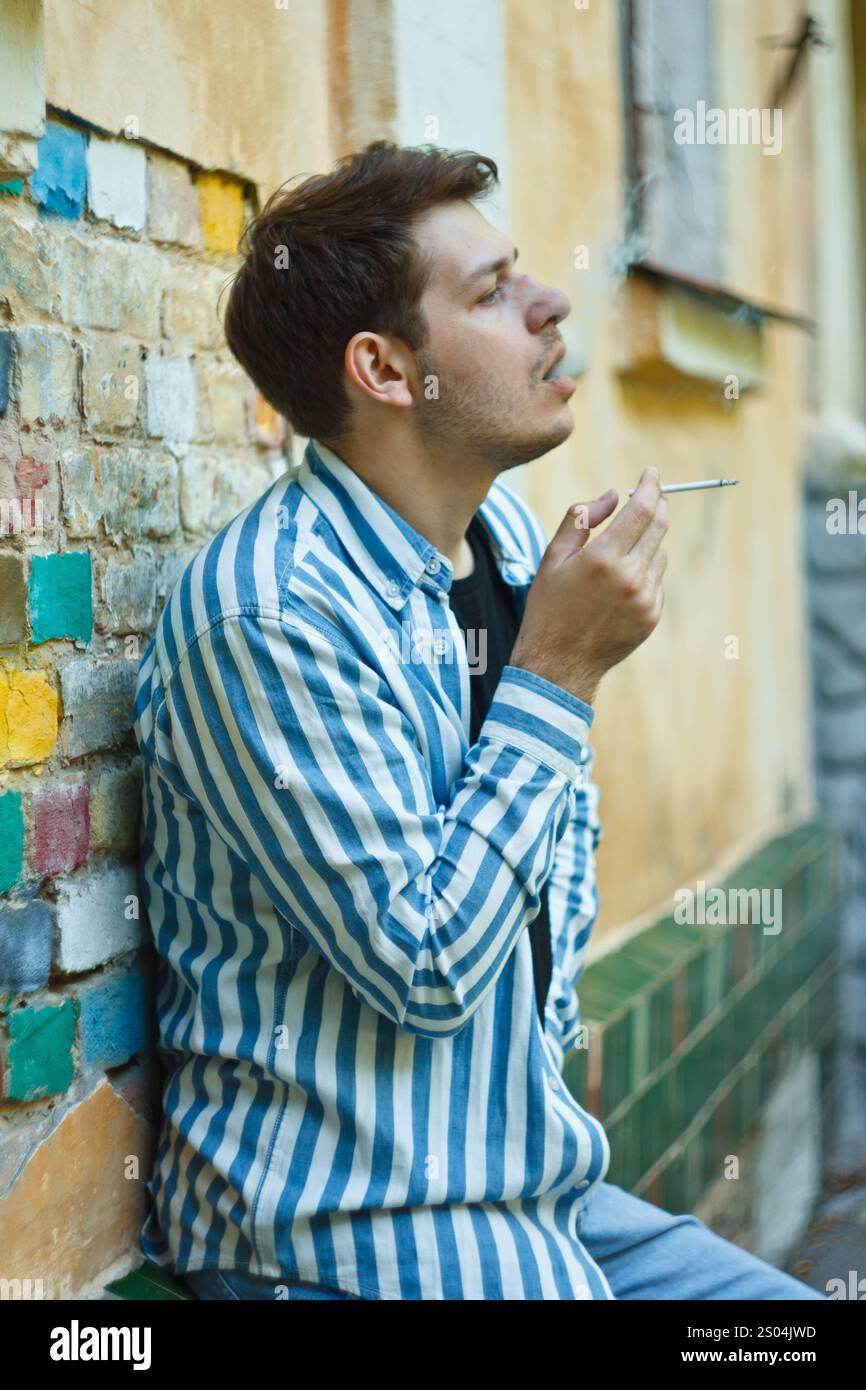 A man leans against an old wall and smokes a cigarette. A minimalist ...