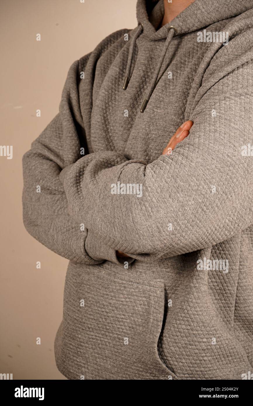 A man in gray clothing stands with arms crossed, creating a closed and ...