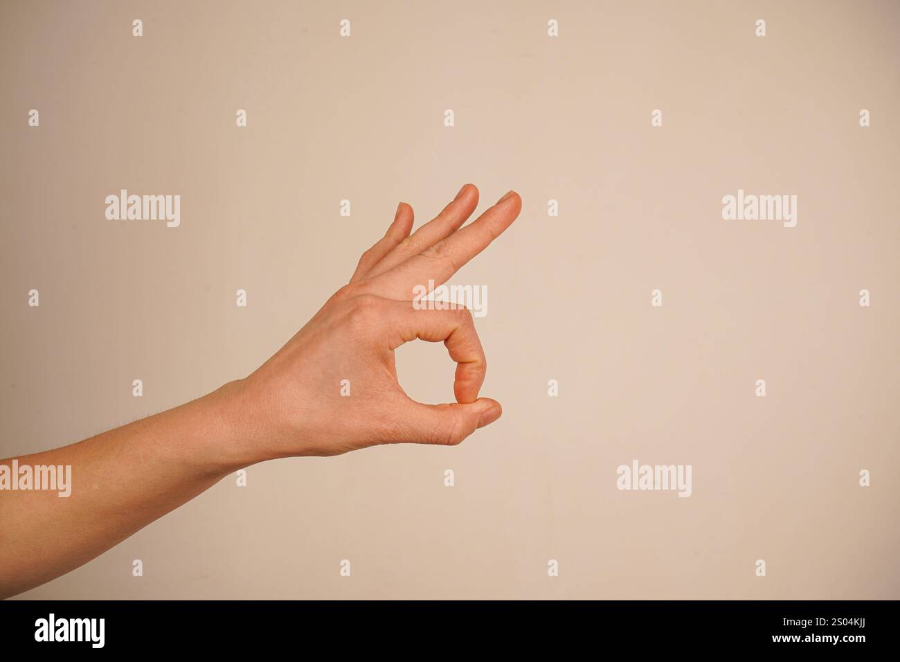 A close-up of a human hand forming an okay gesture against a light wall ...