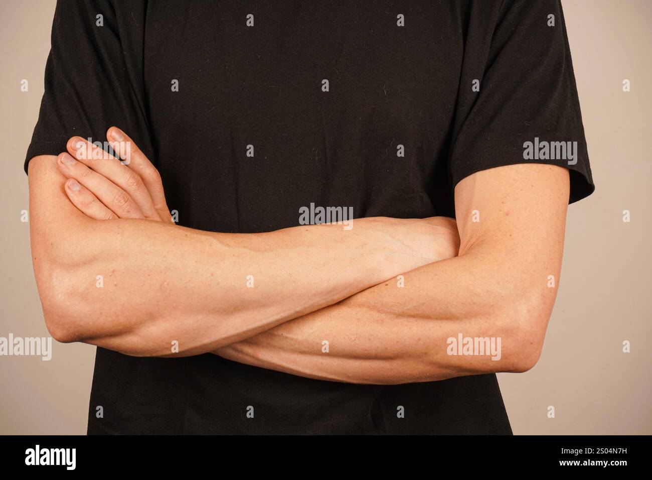 A man folds his arms in a protective pose, hands resting on each other ...