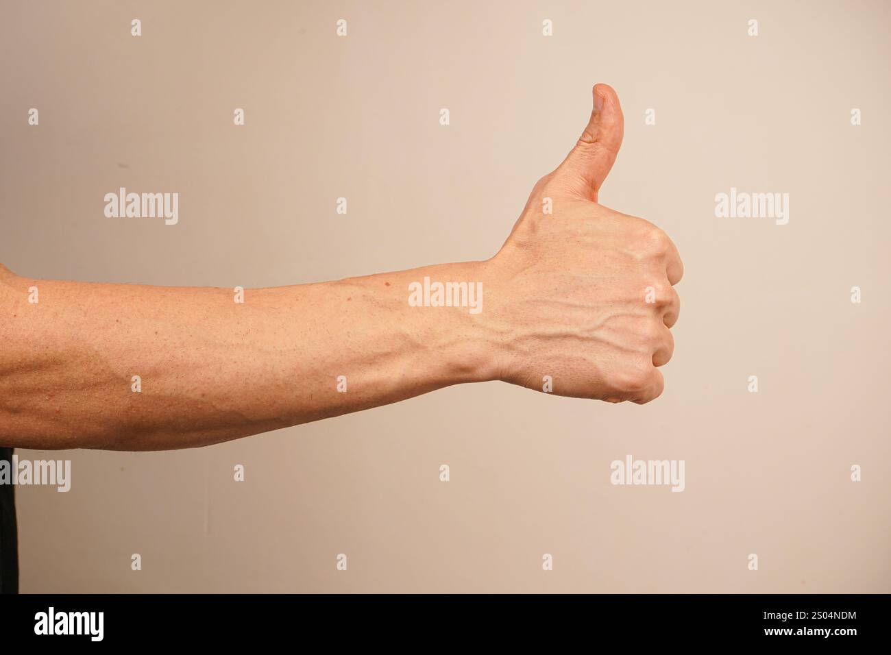 A hand giving a thumbs-up sign against a neutral, bright wall. The ...