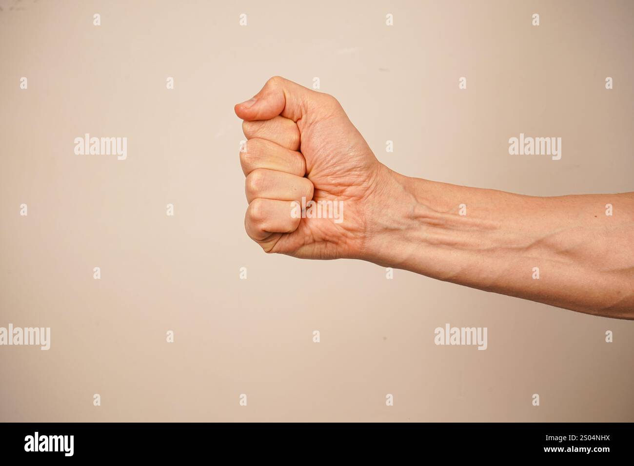 A man clenches his hand tightly into a fist, all the tendons and veins ...
