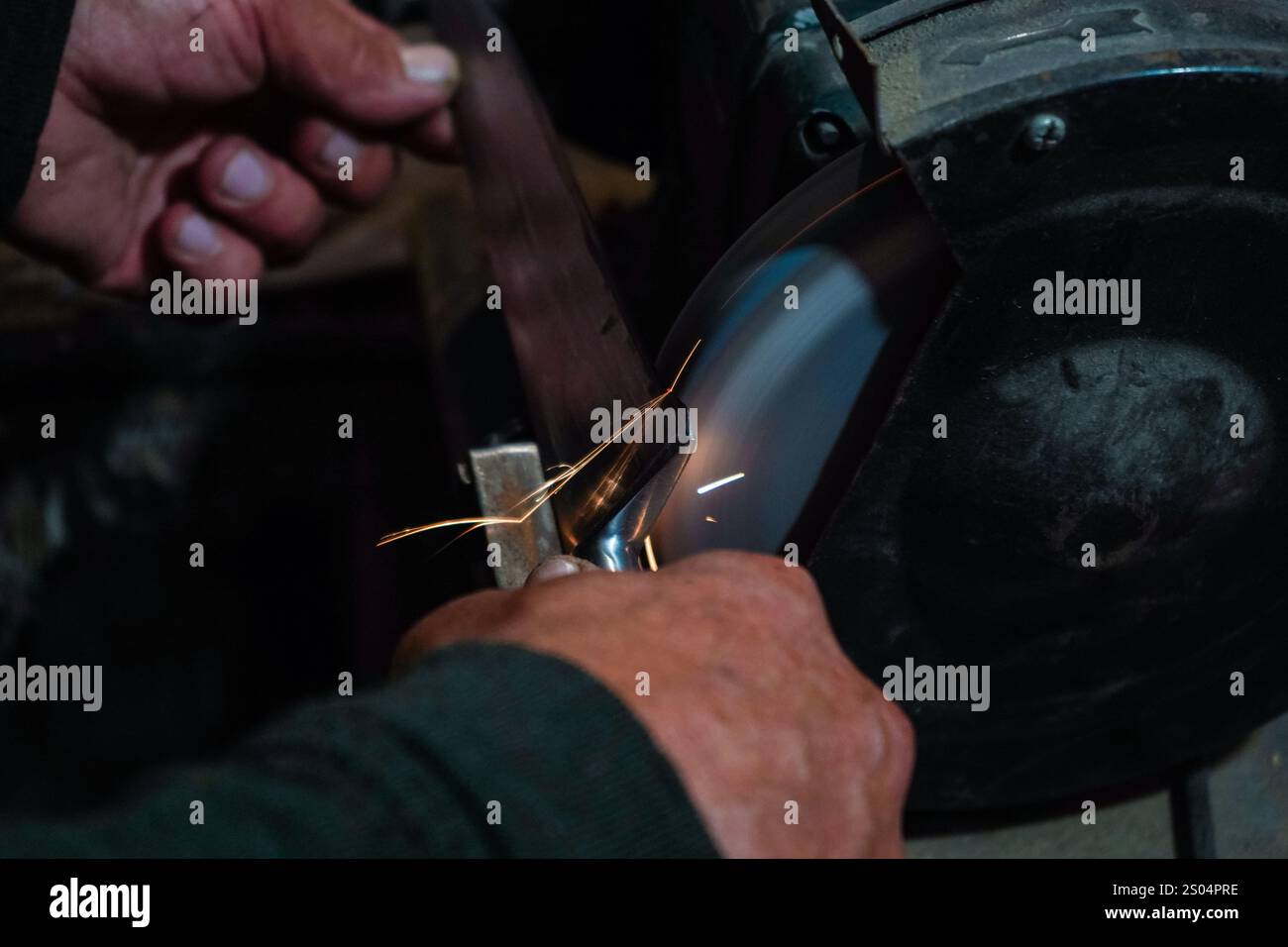 The hands of a skilled craftsman sharpen a metal tool on a rotating ...