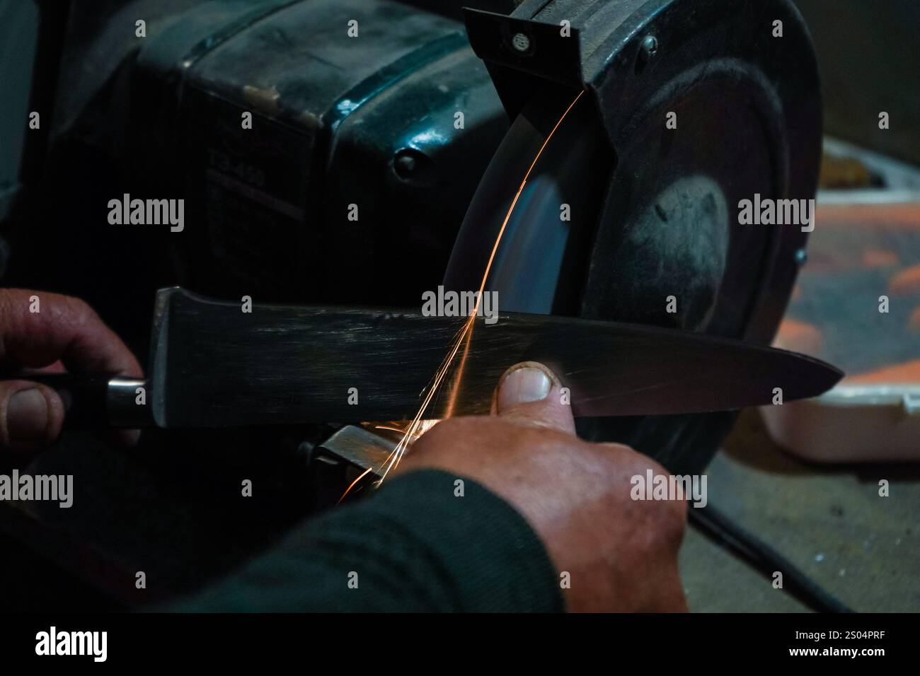A close-up of a craftsman's hands sharpening a metal tool on a grinding ...