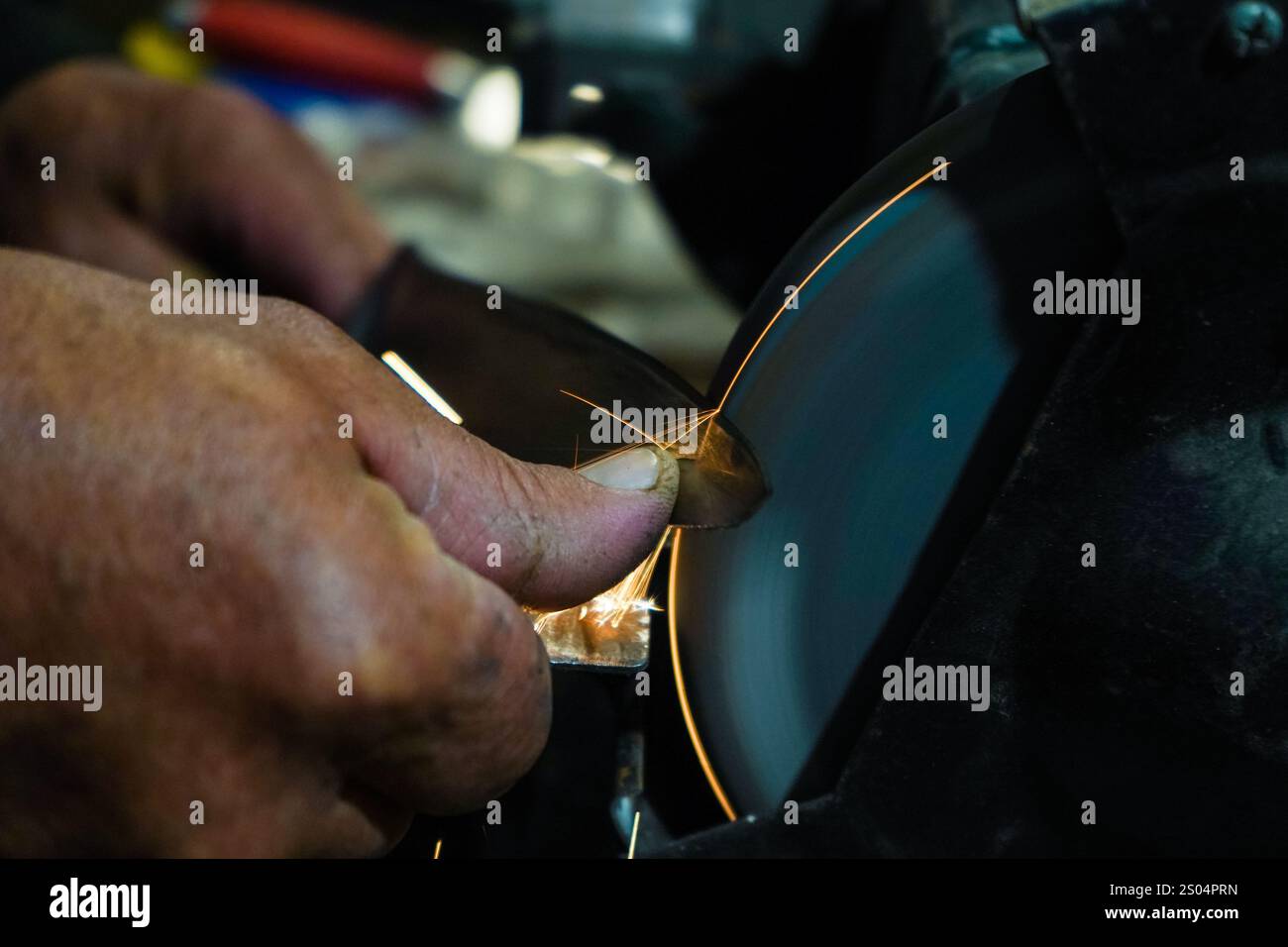 A close-up of a craftsman's hands sharpening a metal tool on a grinding ...