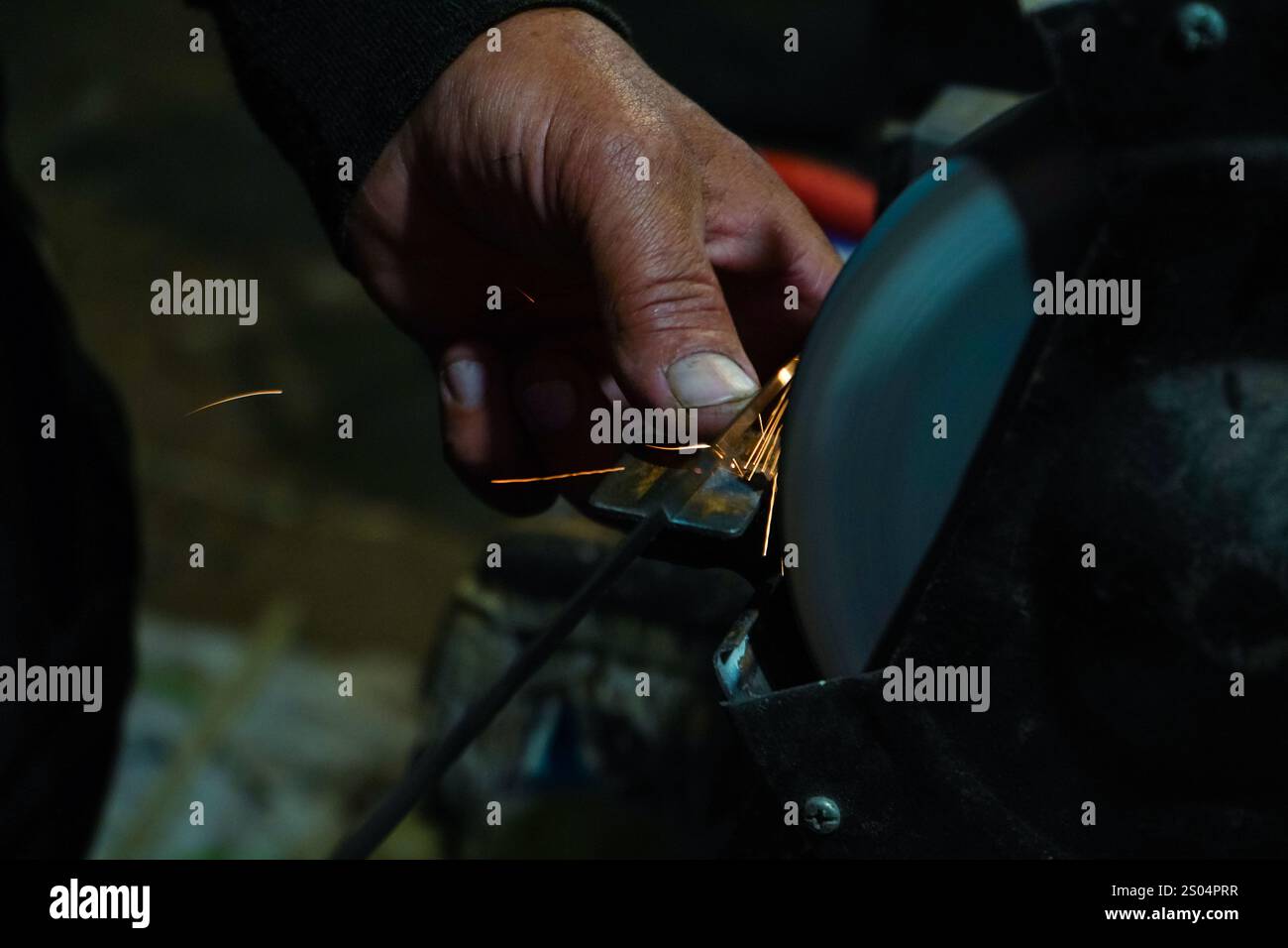 A close-up of a craftsman's hands sharpening a metal tool on a grinding ...