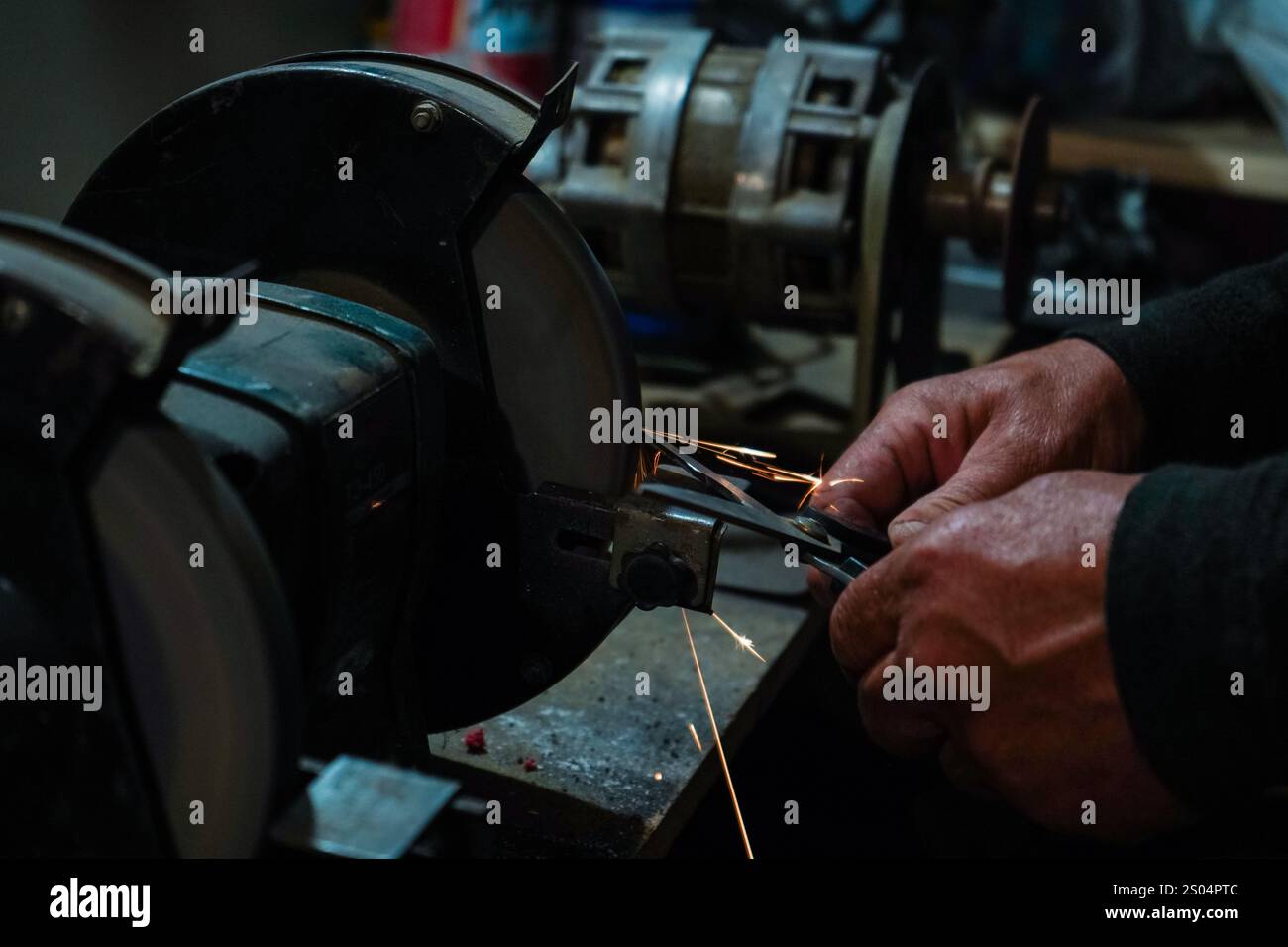 A close-up of a craftsman's hands sharpening a metal tool on a grinding wheel. The friction ...