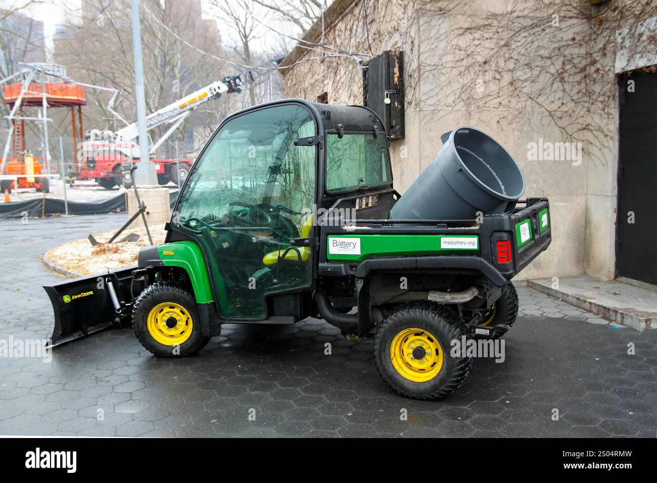 Green utility vehicle equipped with snow plow and salt spreader parked ...