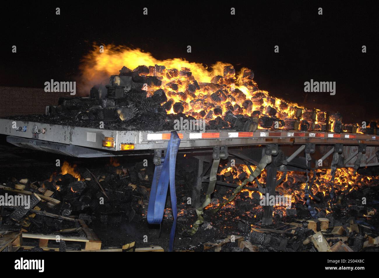 Burning and glowing embers on a flatbed trailer following a pallet yard ...