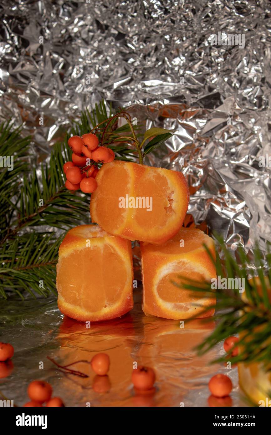 Cubes from iced tangerine and evergreen branches on crumpled aluminium ...