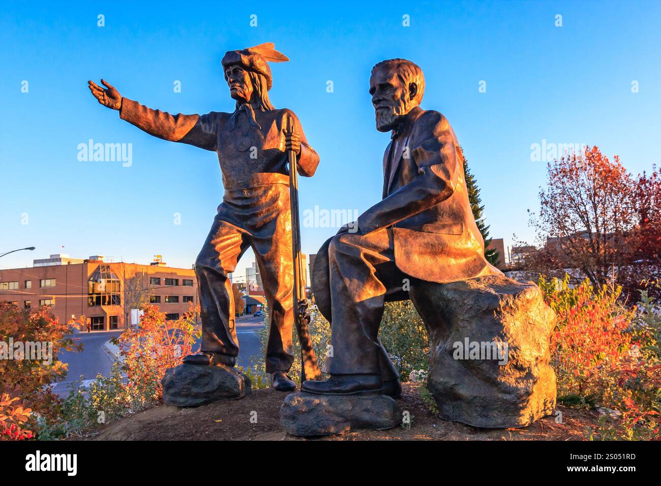 Two statues of men, one of them holding a rifle, are sitting on a rock ...