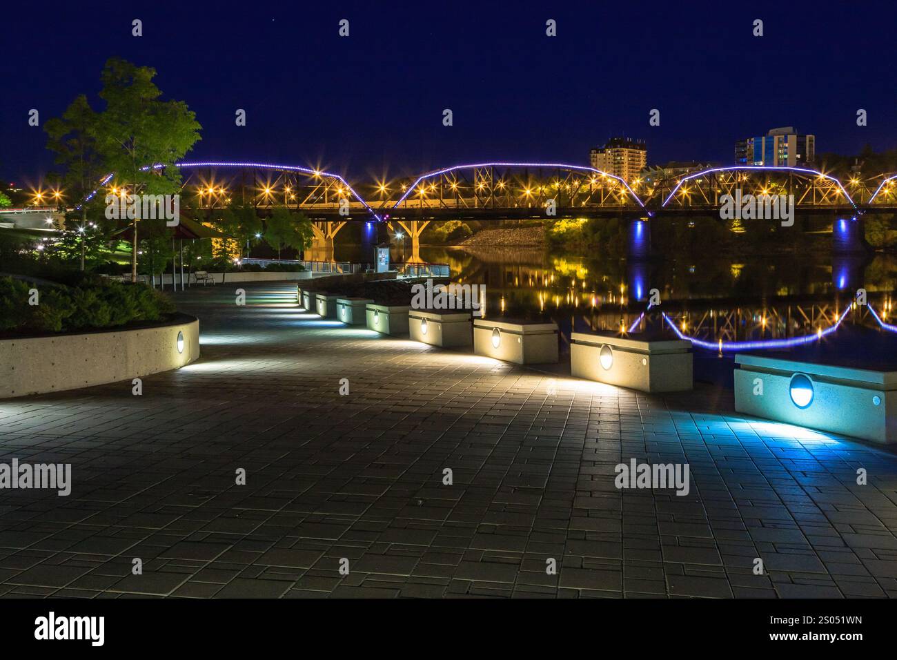 A bridge is lit up at night, with lights reflecting on the water. The ...