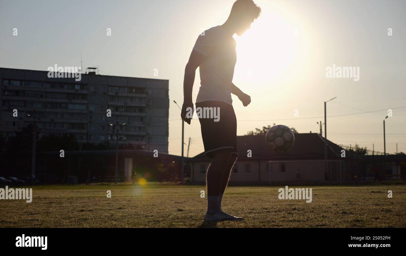 Professional footballer juggling soccer ball on stadium at sunset ...