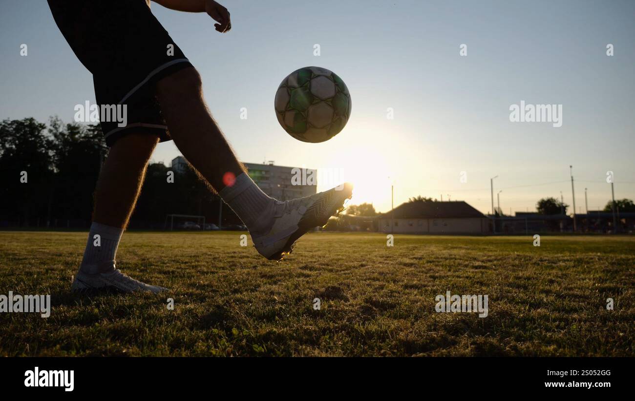 Legs of young man kicking ball at green field. Male feet of ...