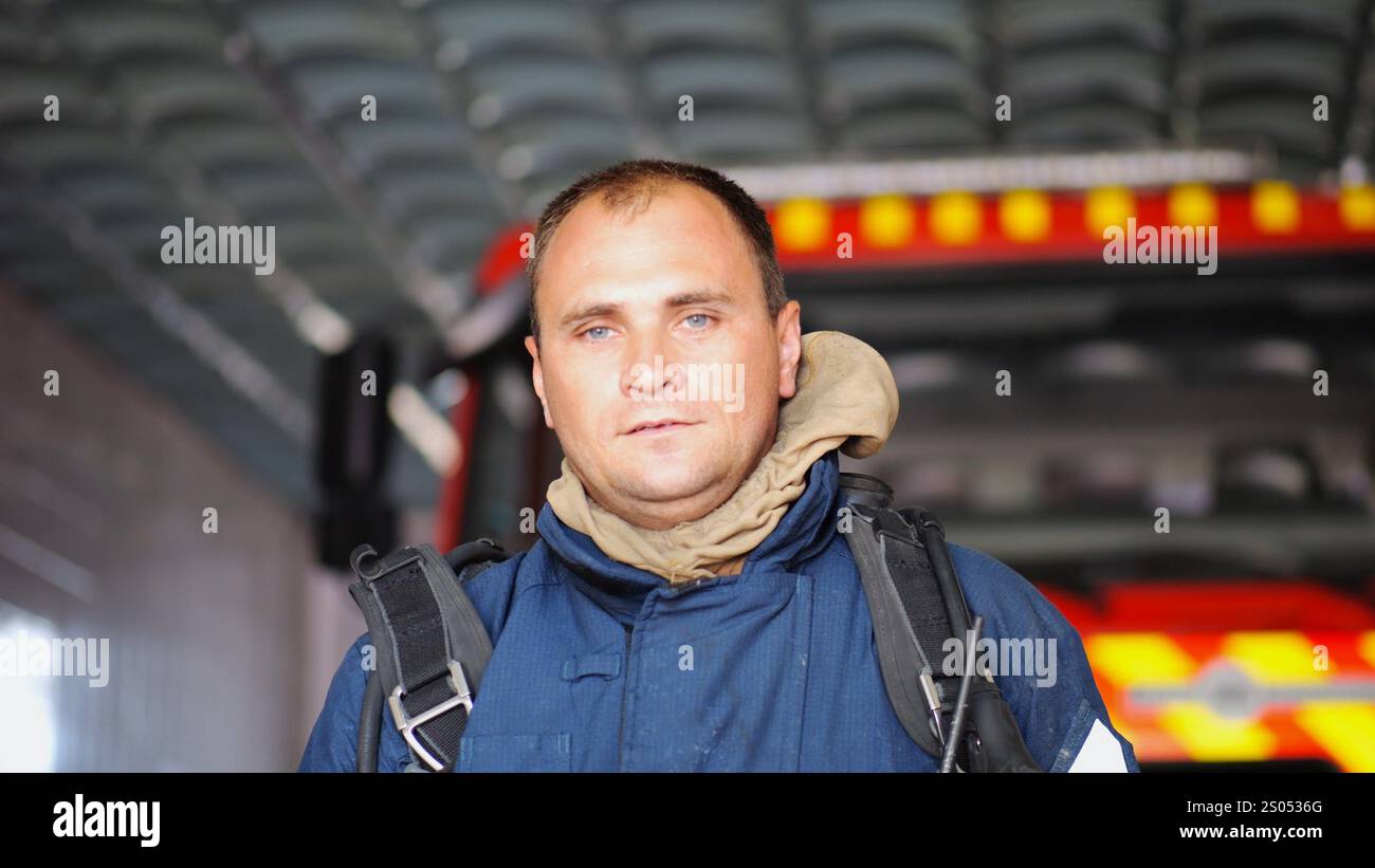 Portrait of tired male firefighter standing near a fire engine at ...