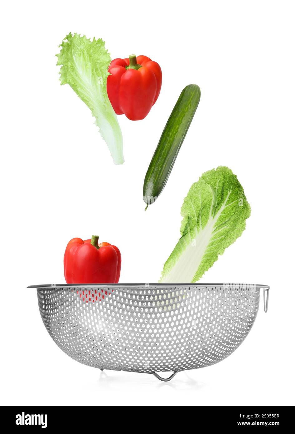 Different fresh vegetables falling into colander on white background ...