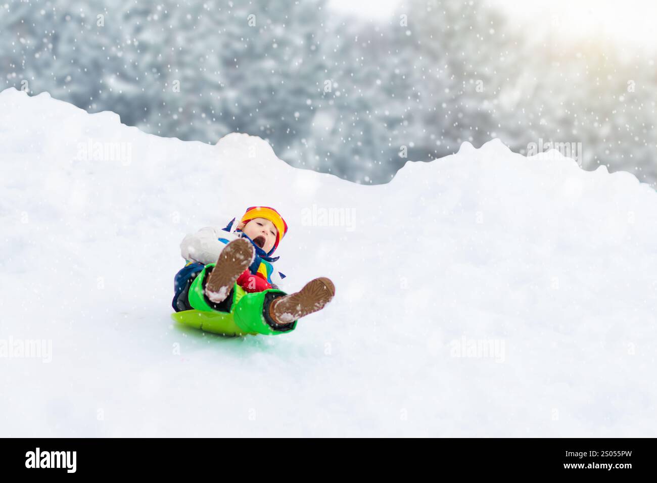 Little girl enjoying a sleigh ride. Child sledding. Toddler kid riding a sledge. Children play ...