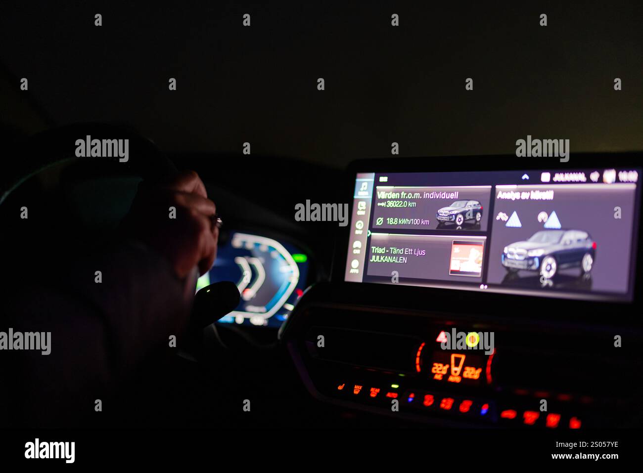 Driver operating BMW iX3 electric car at night, focusing on illuminated infotainment display and ...