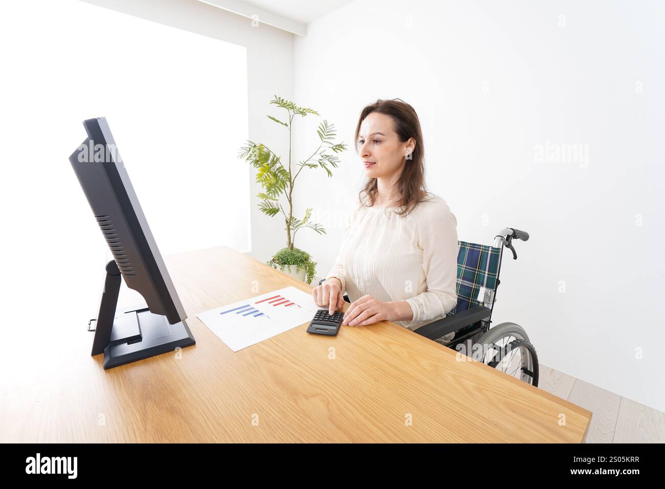 Foreign woman working at a desk in a wheelchair Stock Photo - Alamy