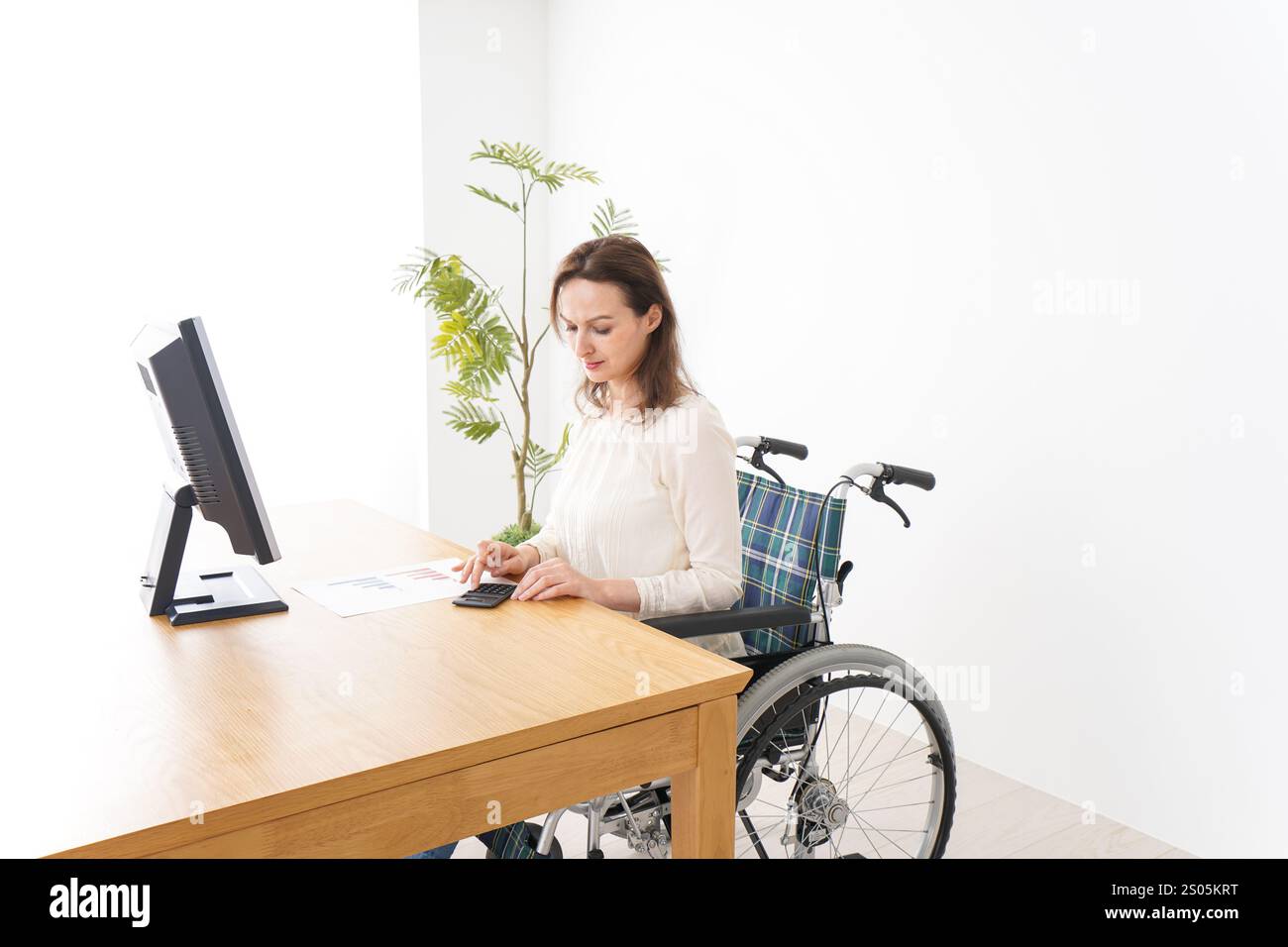 Foreign woman working at a desk in a wheelchair Stock Photo - Alamy