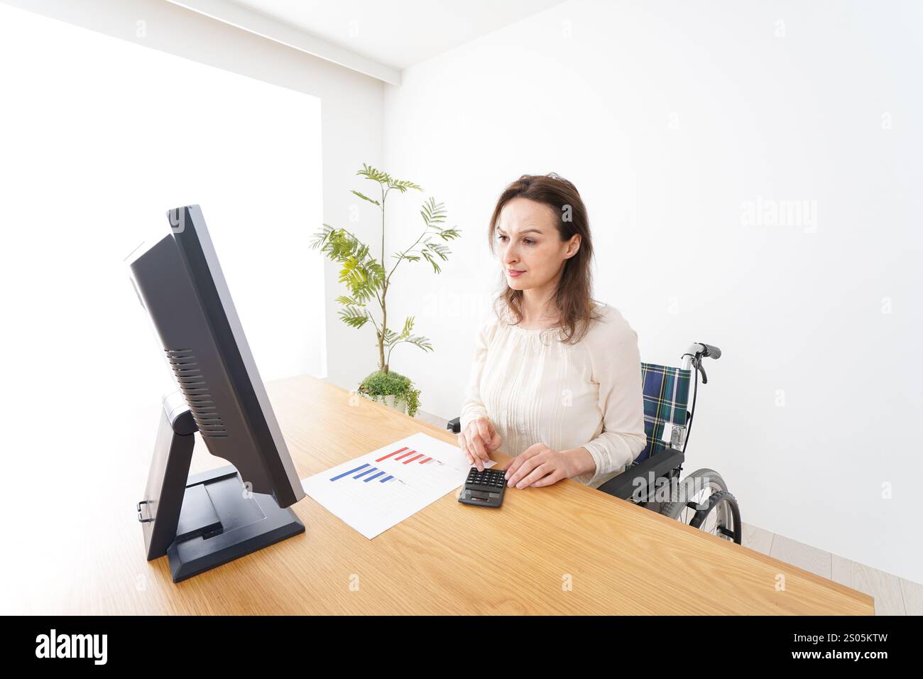 Foreign woman working at a desk in a wheelchair Stock Photo - Alamy