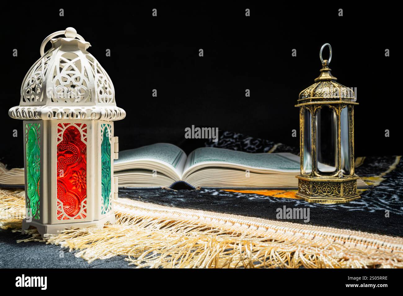 Arabic lanterns and Quran on a prayer mat with a black background ...