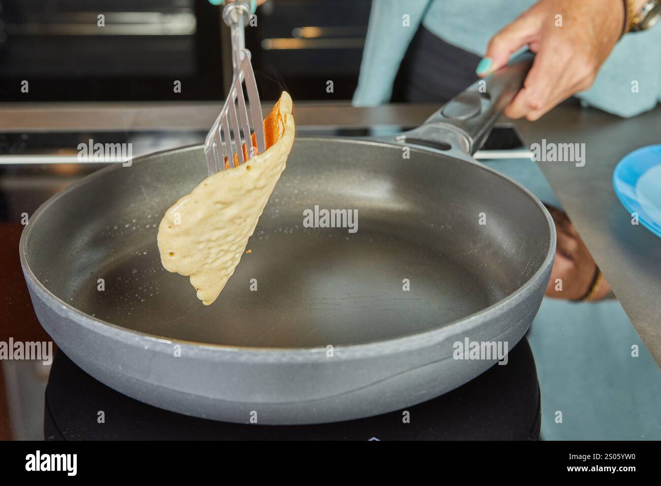 A person flips a golden-brown pancake in a frying pan on the stovetop ...