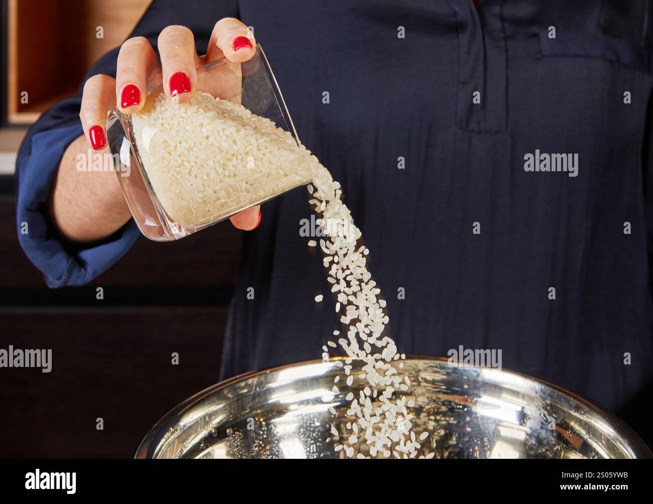 A close-up of hands pouring uncooked sushi rice from a glass into a ...