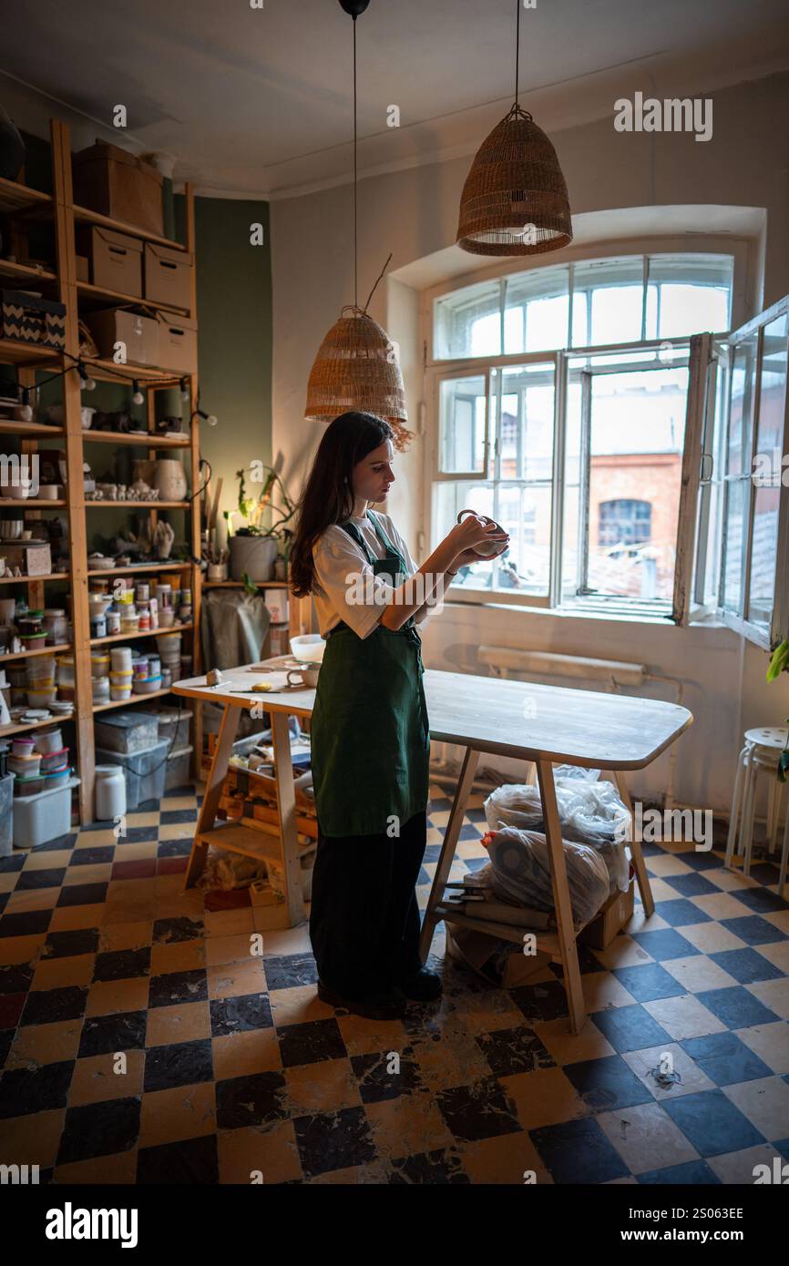 Female artisan examining freshly made clay cup, evaluating form and ...