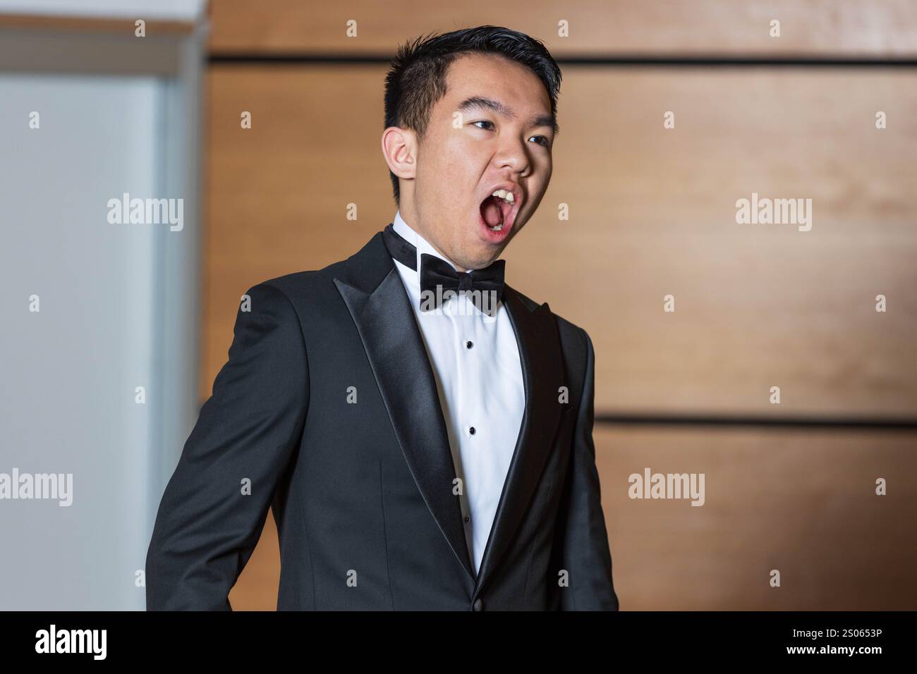 A young teenage boy dressed in a tuxedo and bow tie is standing on ...