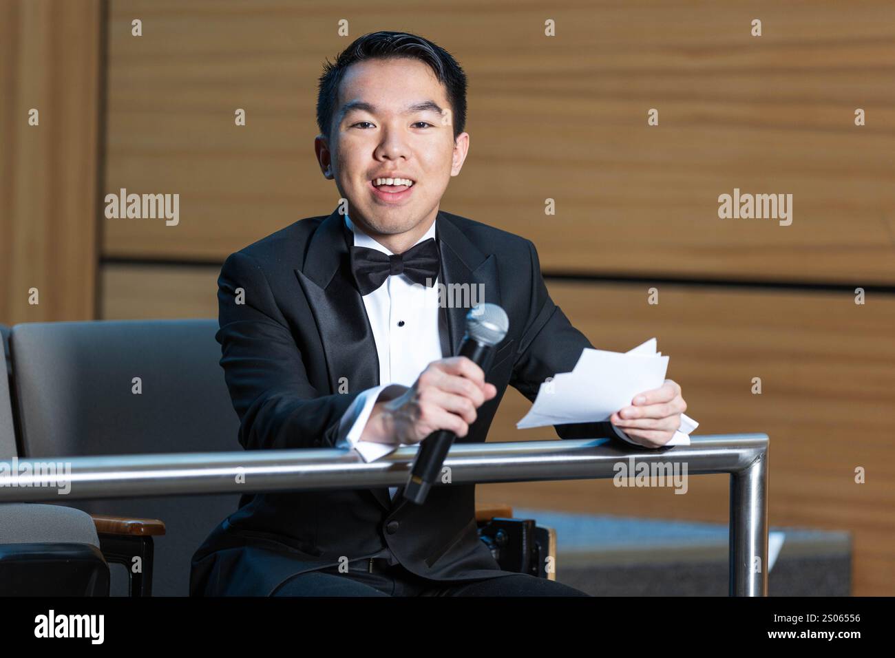 A young university student is at a public speaking competition, seated ...