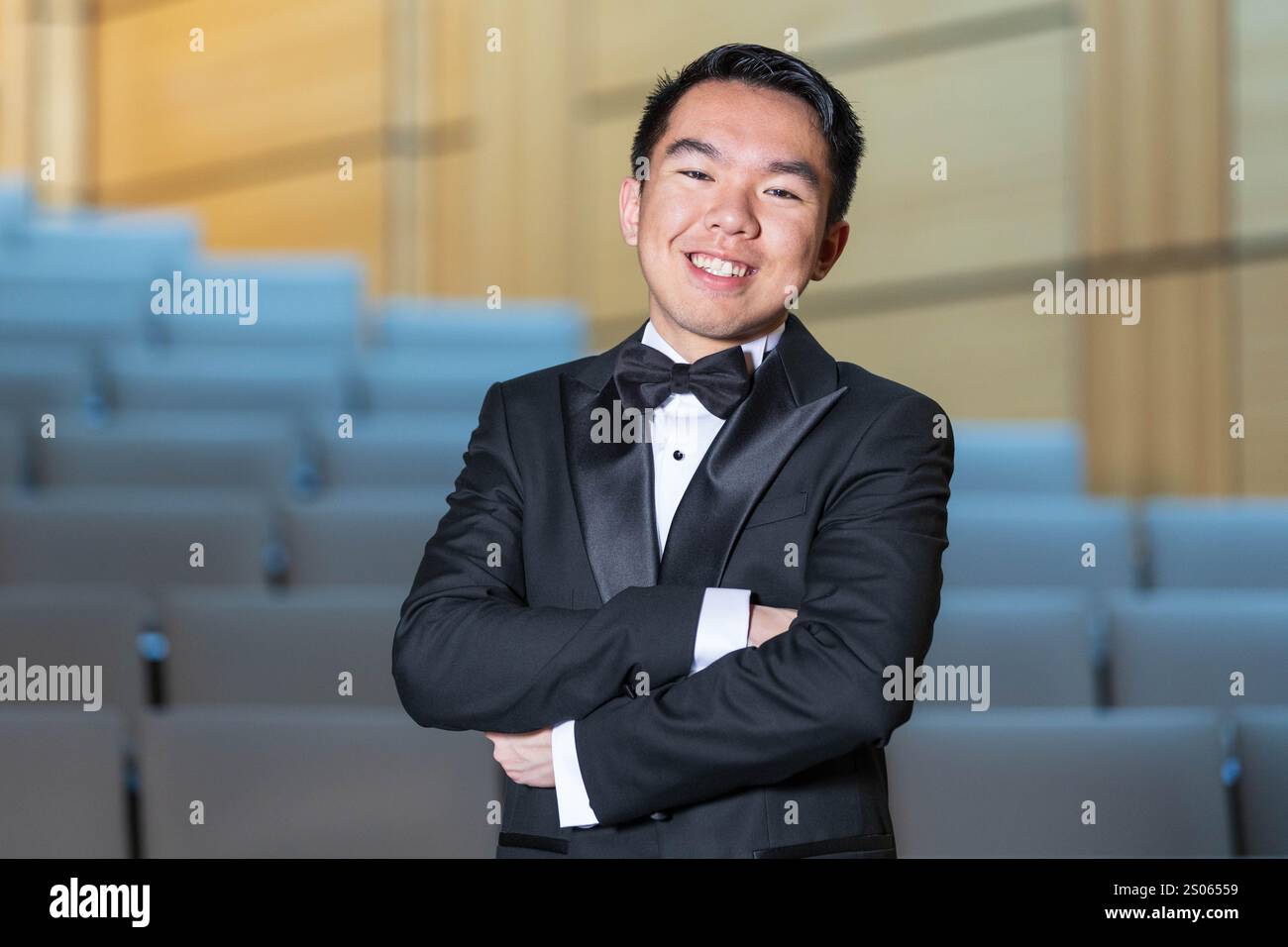 A young man in a tuxedo with a bow tie is grinning while standing in an ...