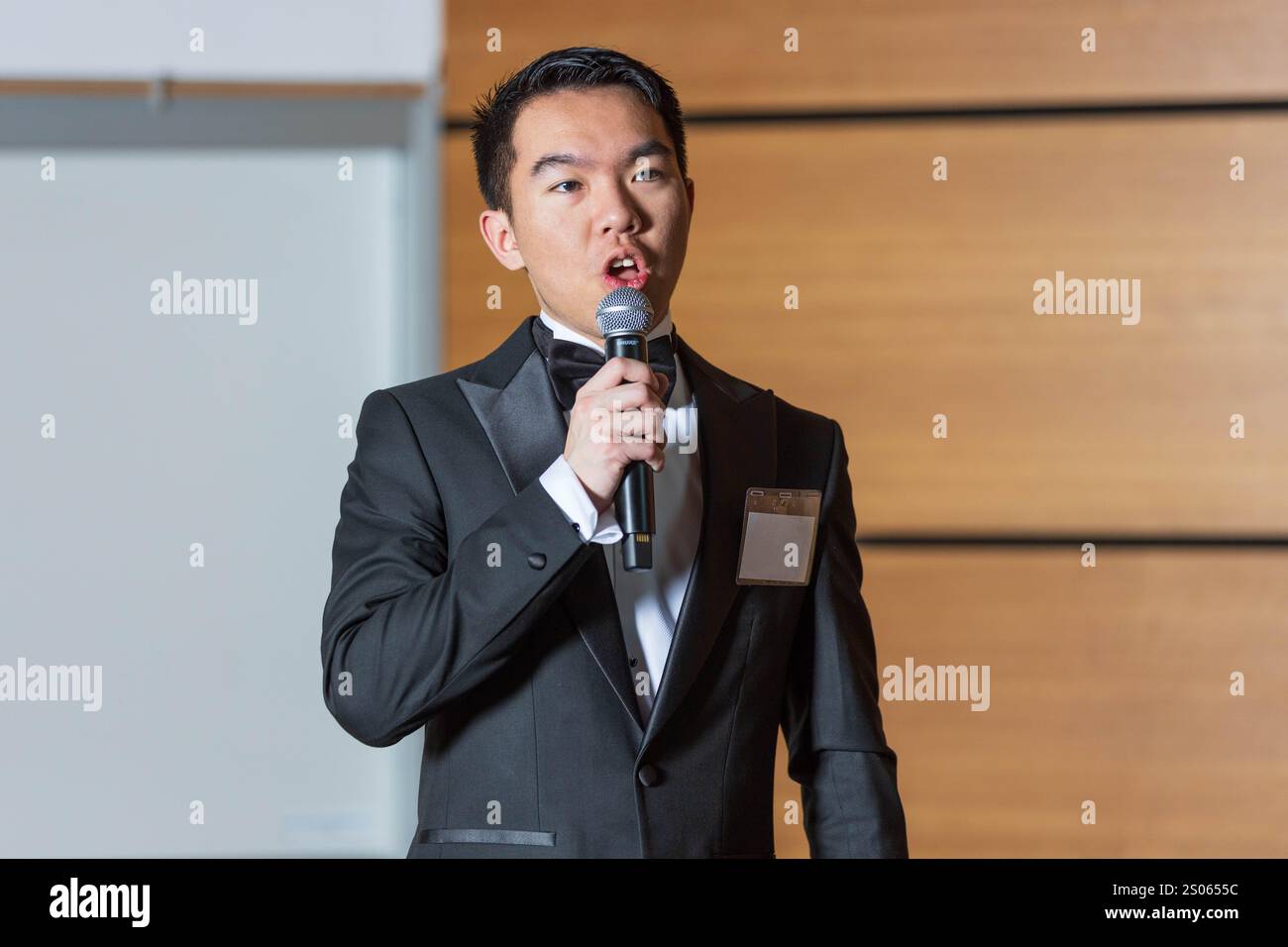 A young man is giving a speech on stage confidently, holding a ...