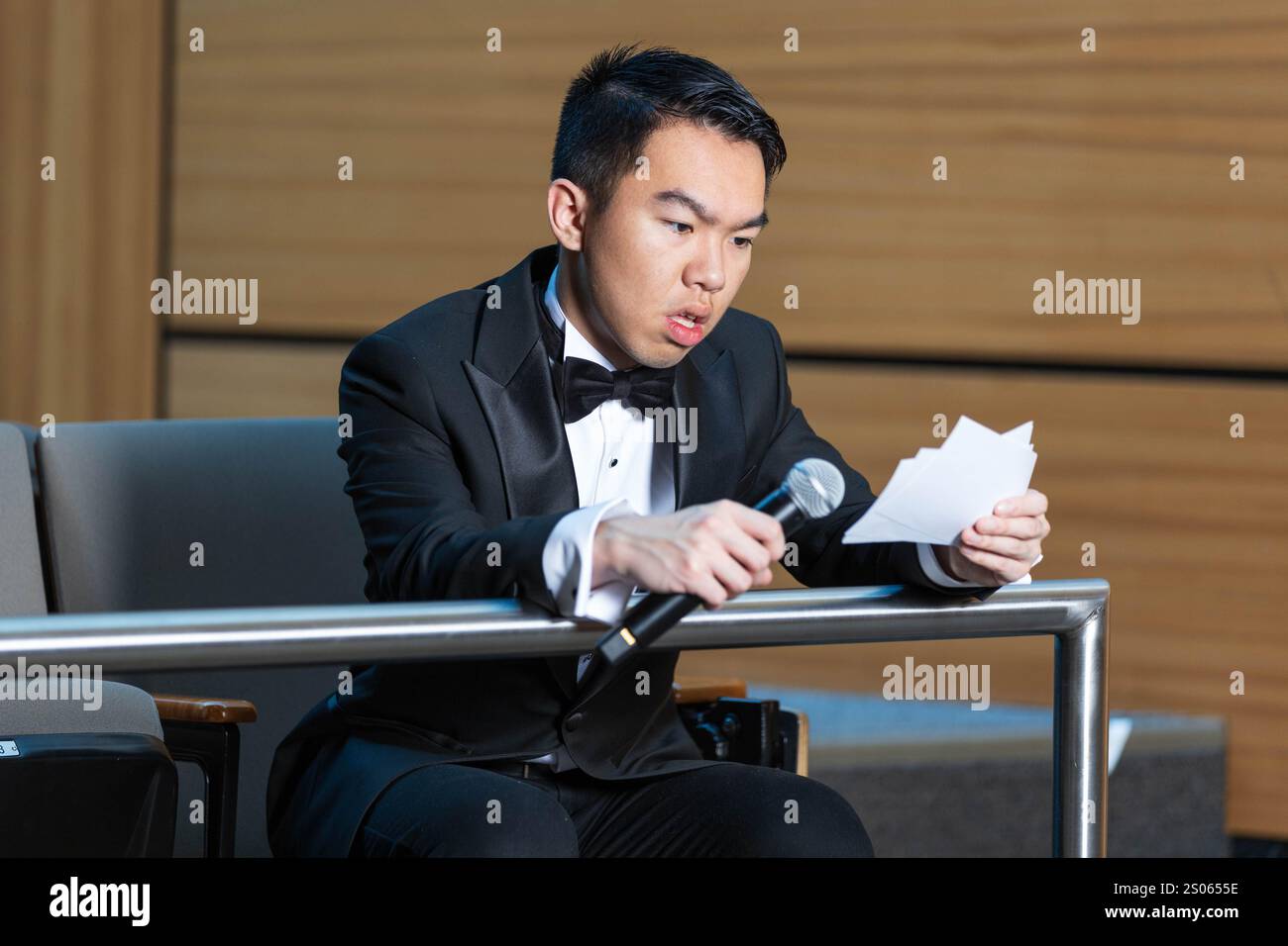 A young university student is at a public speaking competition, seated ...