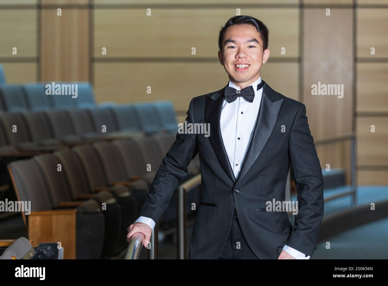 A young man in a tuxedo with a bow tie is grinning while standing in an ...
