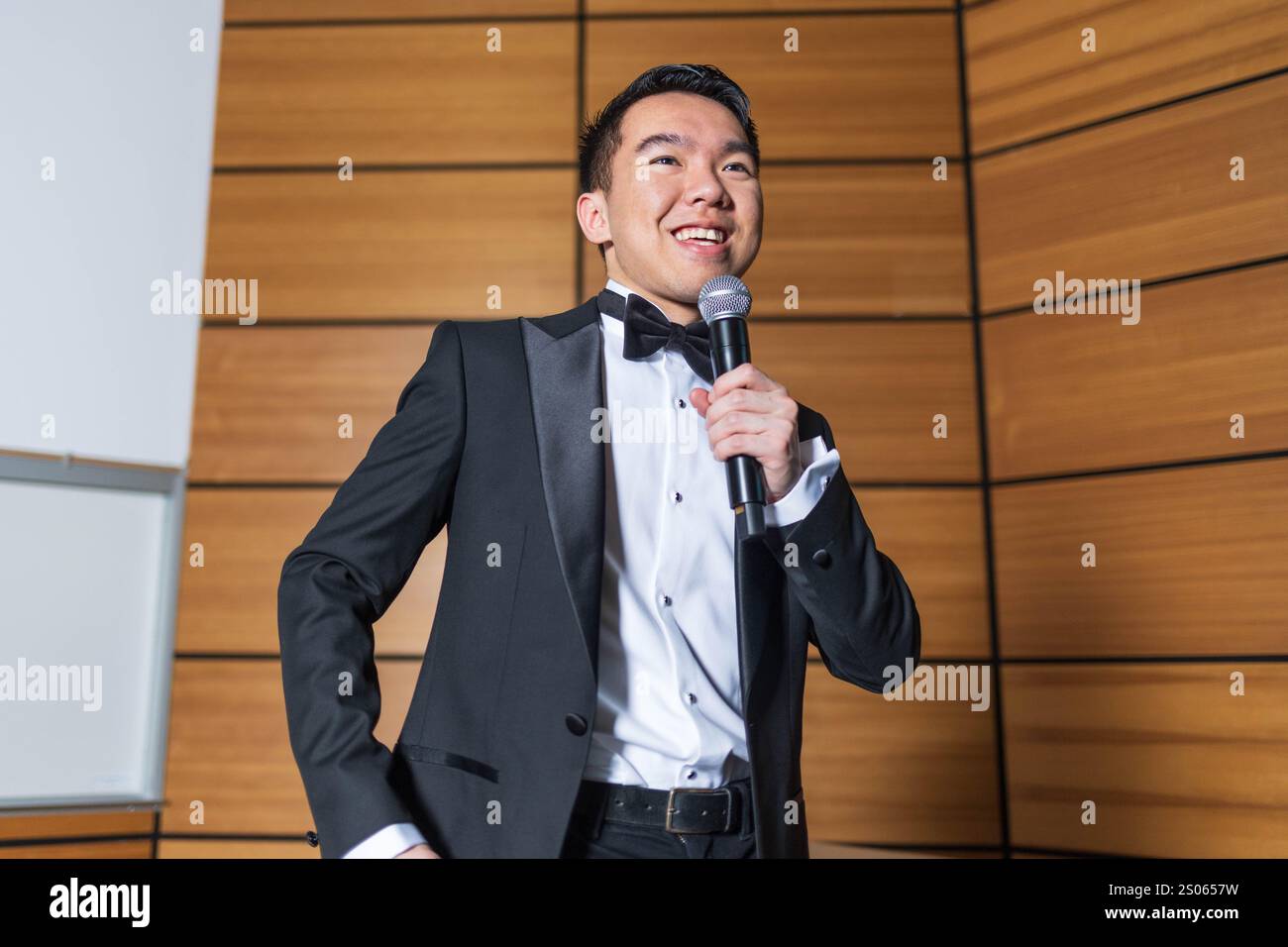 A young man is giving a speech on stage holding a microphone as an ...
