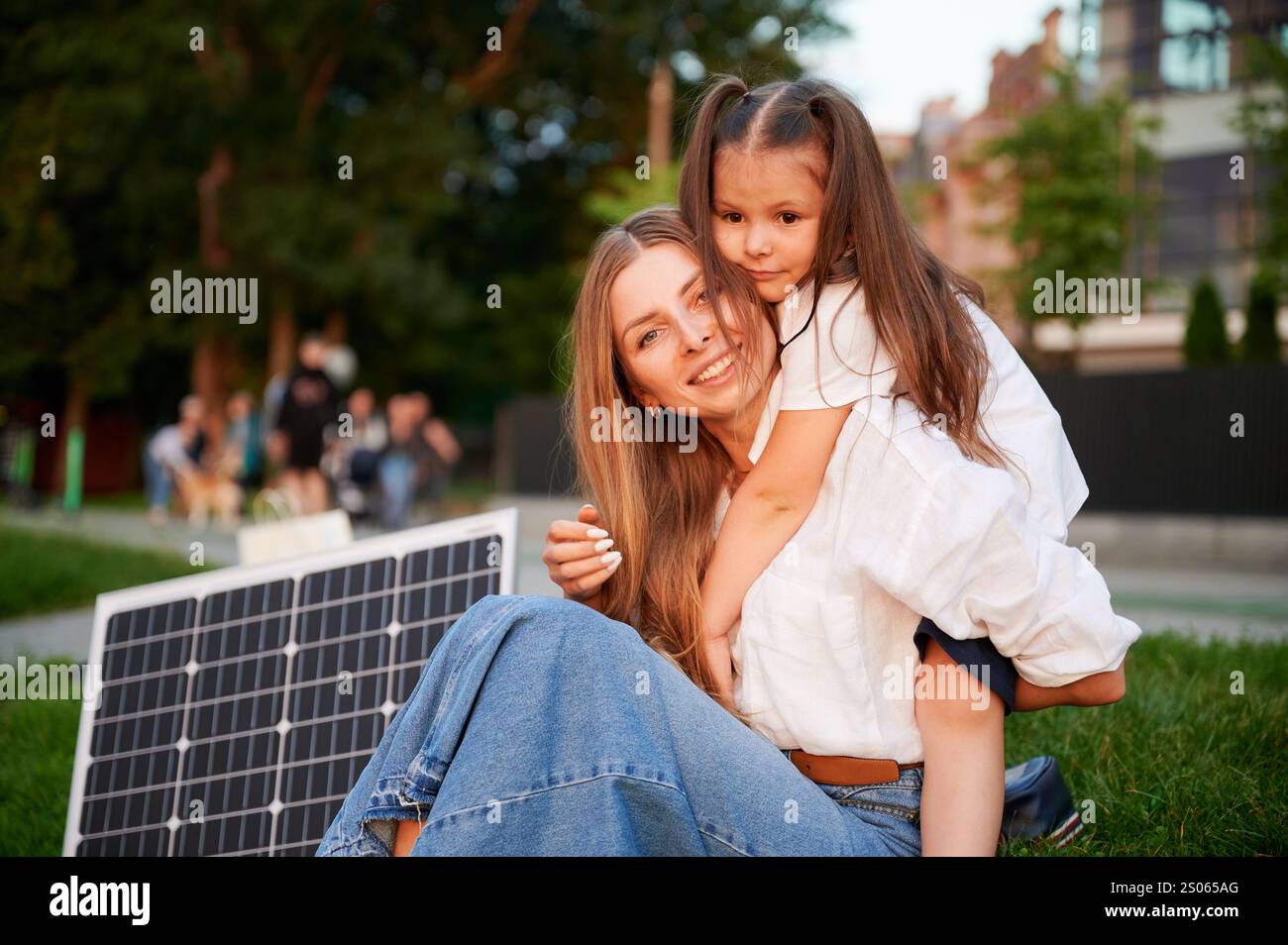 Mother and daughter sit together on grass, embracing in warm moment ...